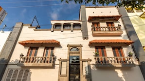 Um edifício com entrada central, varandas com grades e uma placa indicando ser um hotel.