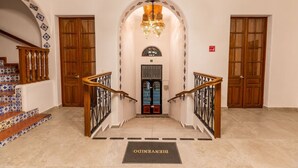 Uma escadaria imponente com um candelabro, portas de madeira e um tapete de entrada com o nome 'BINGHARD'.