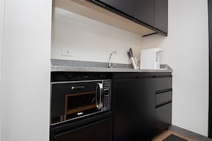 Uma cozinha compacta com forno embutido, cafeteira e micro-ondas.