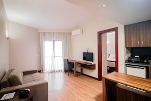 Espaço compacto para viver, com sofá, escrivaninha, televisão e pequeno espaço de cozinha.