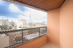 Uma varanda com grade de arame, piso de azulejos e vista para a cidade.
