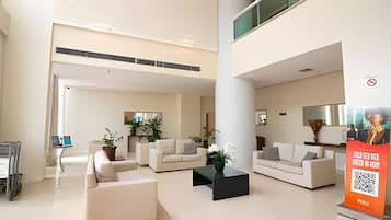 Um hall amplo com pé direito alto, uma coluna central e duas áreas de estar com sofás e uma mesa de centro.