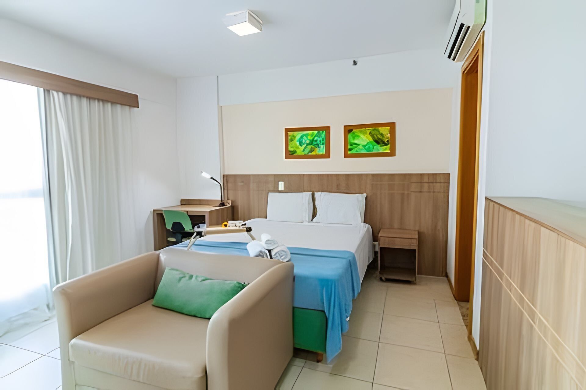 Quarto de hotel com uma cama, escrivaninha, cadeira e uma pequena mesa.