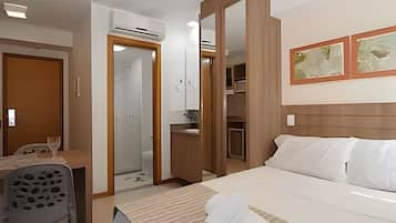 Quarto de hotel com cama, escrivaninha, cadeira, guarda-roupa e banheiro.