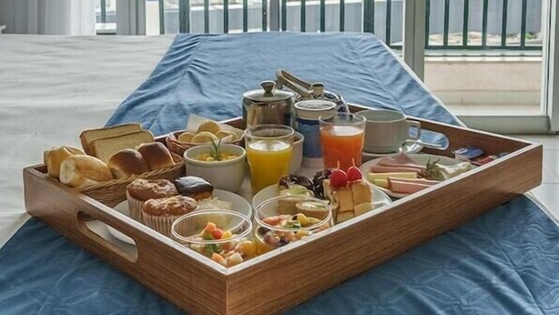 Uma bandeja de café da manhã com diversos alimentos e bebidas sobre a cama em um quarto de hotel com varanda.