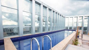 Piscina interior moderna com paredes de vidro transparente, piso azulejado em azul e escada de metal.