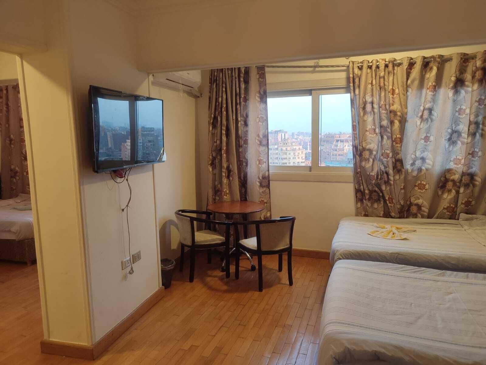 Quarto de hotel com uma cama, uma escrivaninha com cadeira, televisão e janela com cortinas.