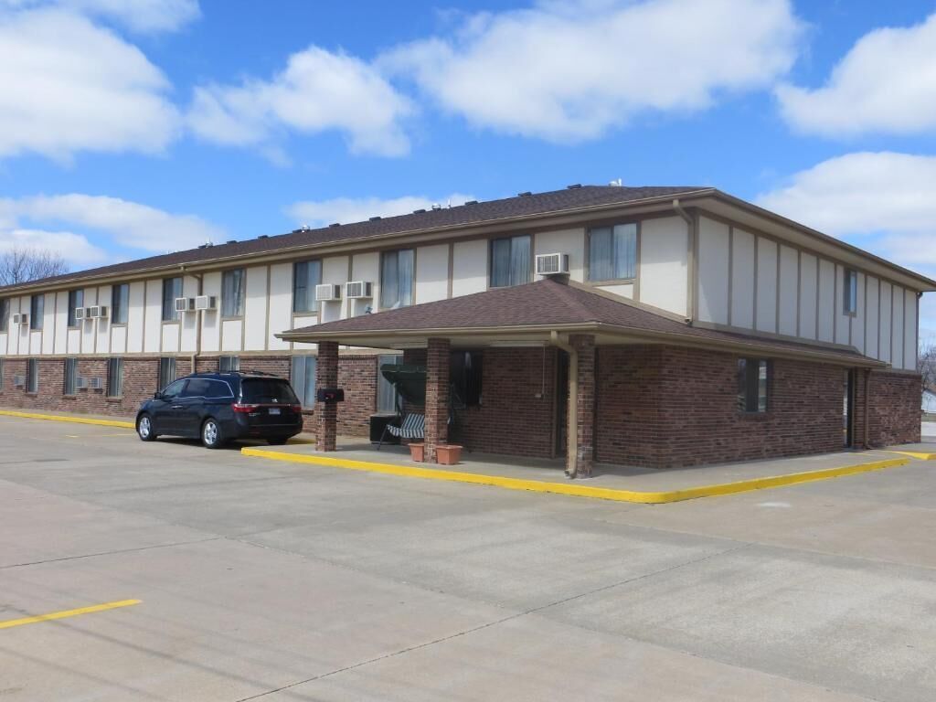 Um motel de dois andares com área de estacionamento coberta e um anexo térreo.