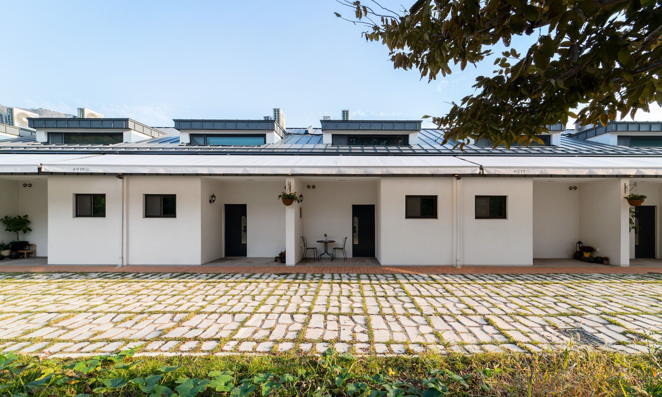Um edifício moderno com telhado plano, várias janelas e um pátio pavimentado.