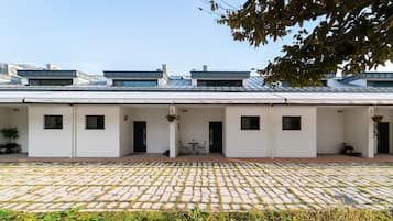 Um edifício moderno com telhado plano, várias janelas e um pátio pavimentado.