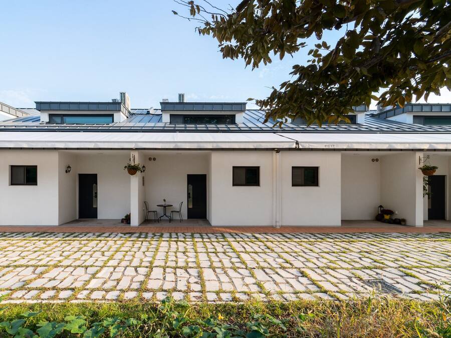 Um edifício moderno com telhado plano, várias janelas e um pátio pavimentado.