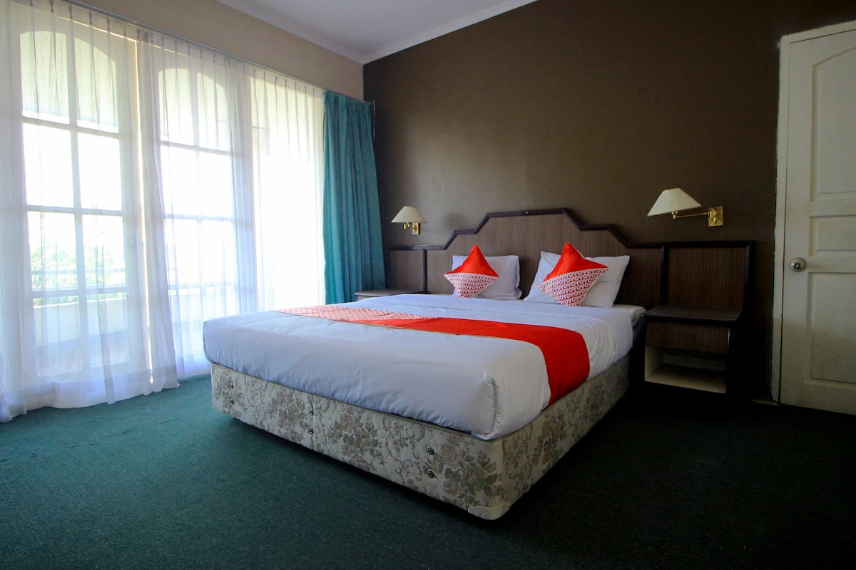Quarto de hotel com cama grande, duas luminárias de cabeceira, mesa de cabeceira e uma porta.