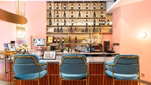 Uma área de bar com três banquetas azuis, um espaço para vinhos com várias garrafas e uma máquina de café.