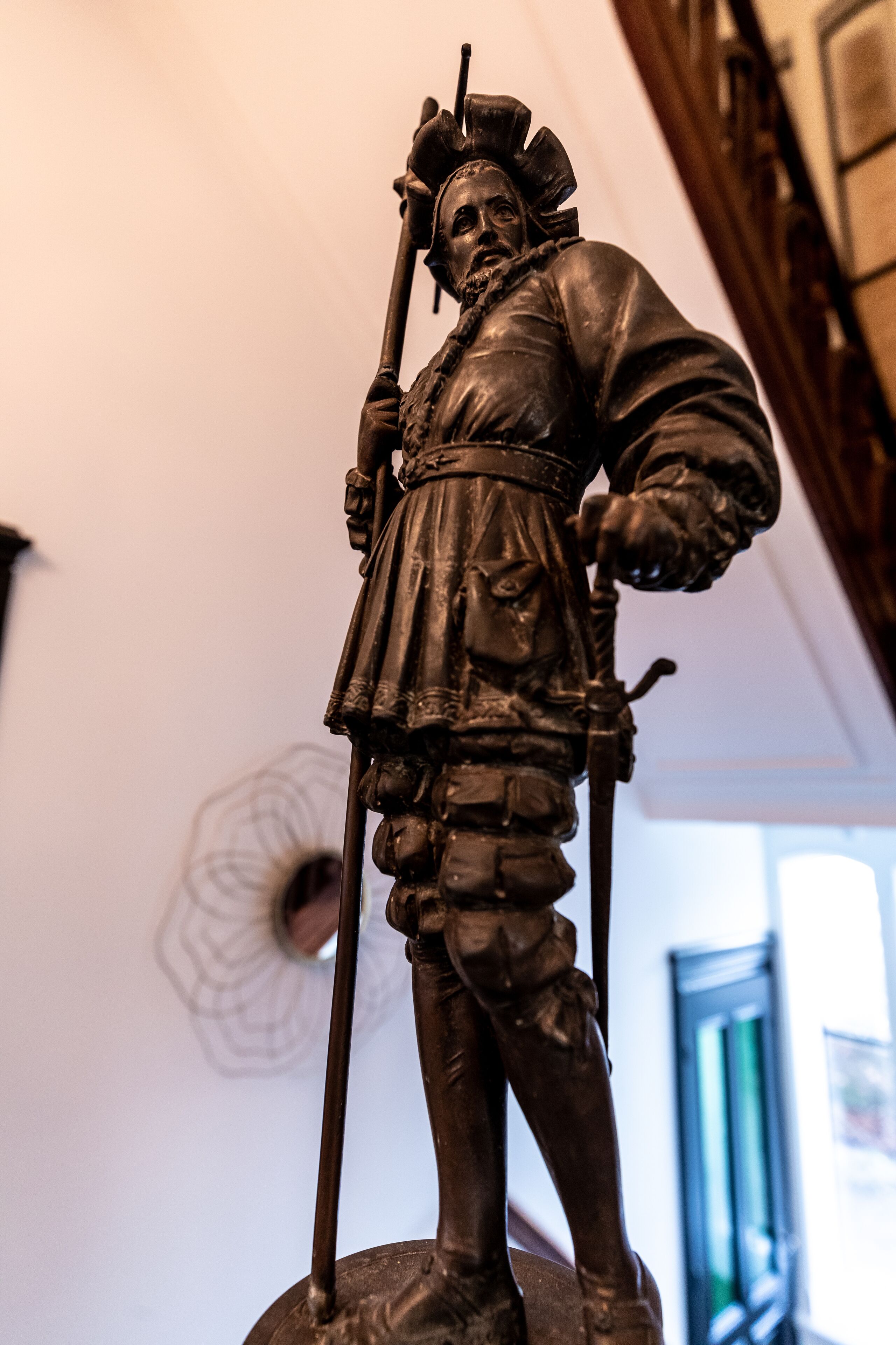 Estátua de uma figura histórica com um bastão, sobre um pedestal.