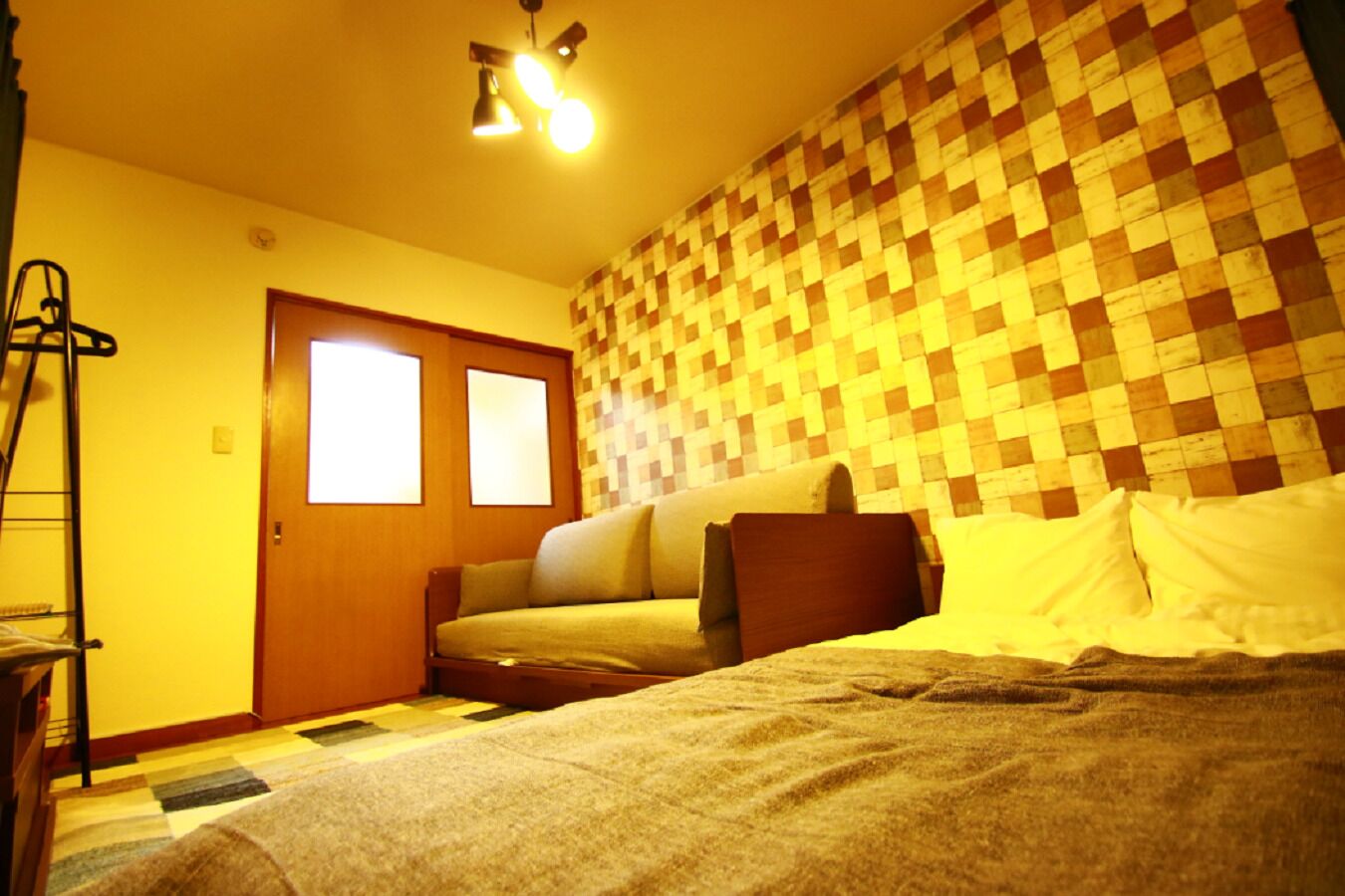 Quarto com cama, sofá, porta de madeira e parede quadriculada.