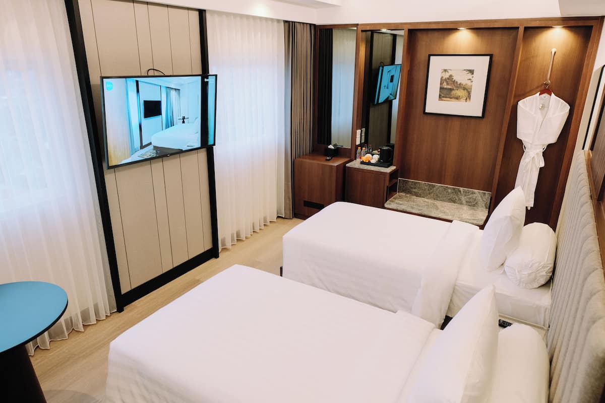 Quarto de hotel com duas camas, televisão, espelho, pequena mesa e roupão pendurado em um gancho.