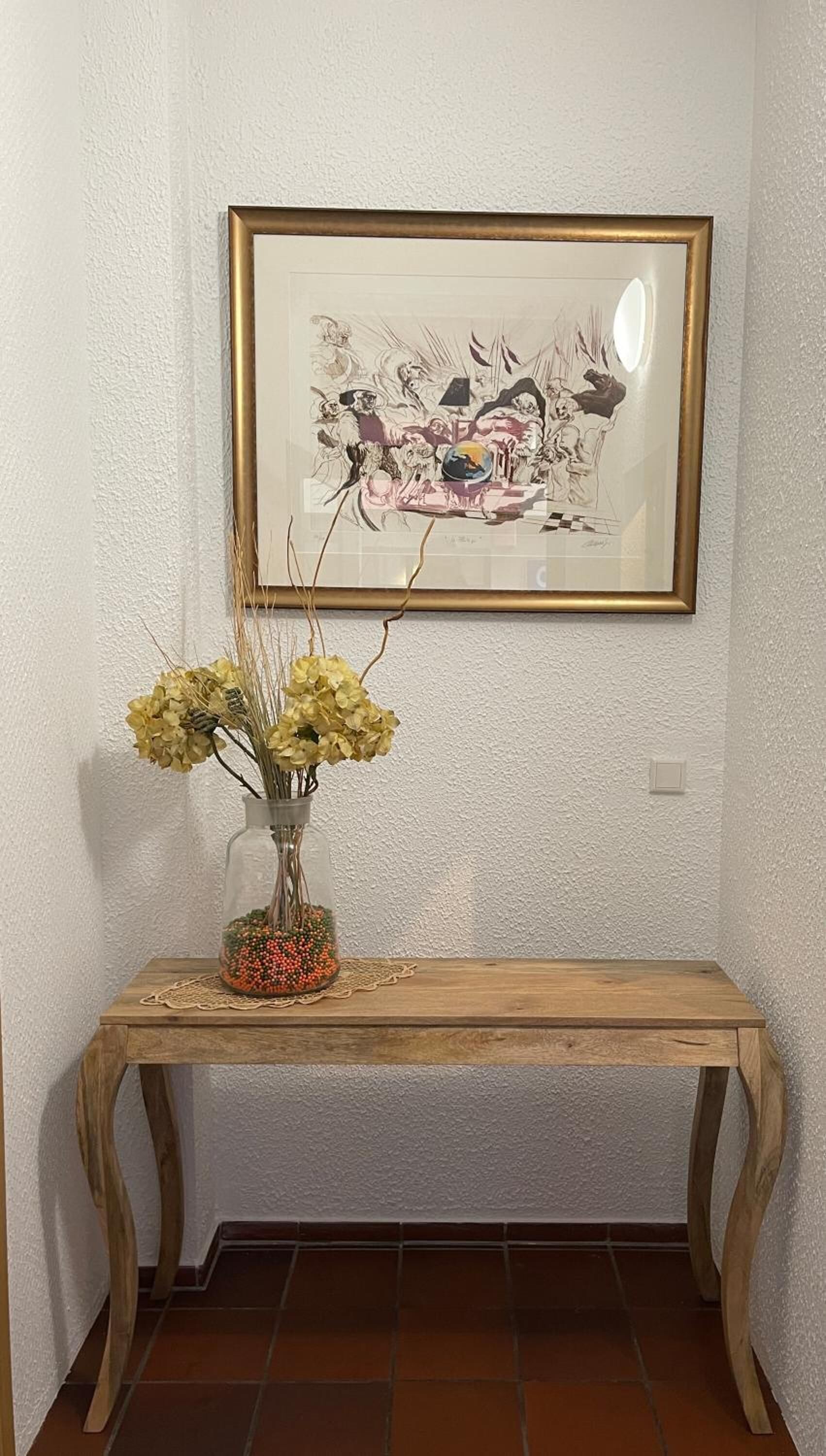 Um banco de madeira com um vaso de flores e uma moldura com uma obra de arte acima.