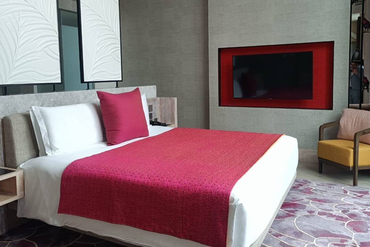 Quarto de hotel moderno com uma cama grande, um cobertor vermelho e um quadro com moldura vermelha na parede.