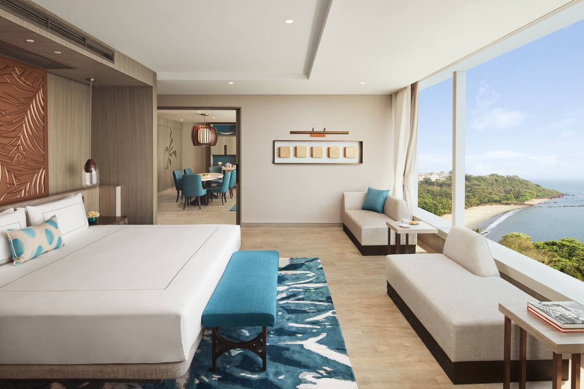 Quarto de hotel moderno com uma cama grande, um sofá, área de jantar e vista para o oceano.