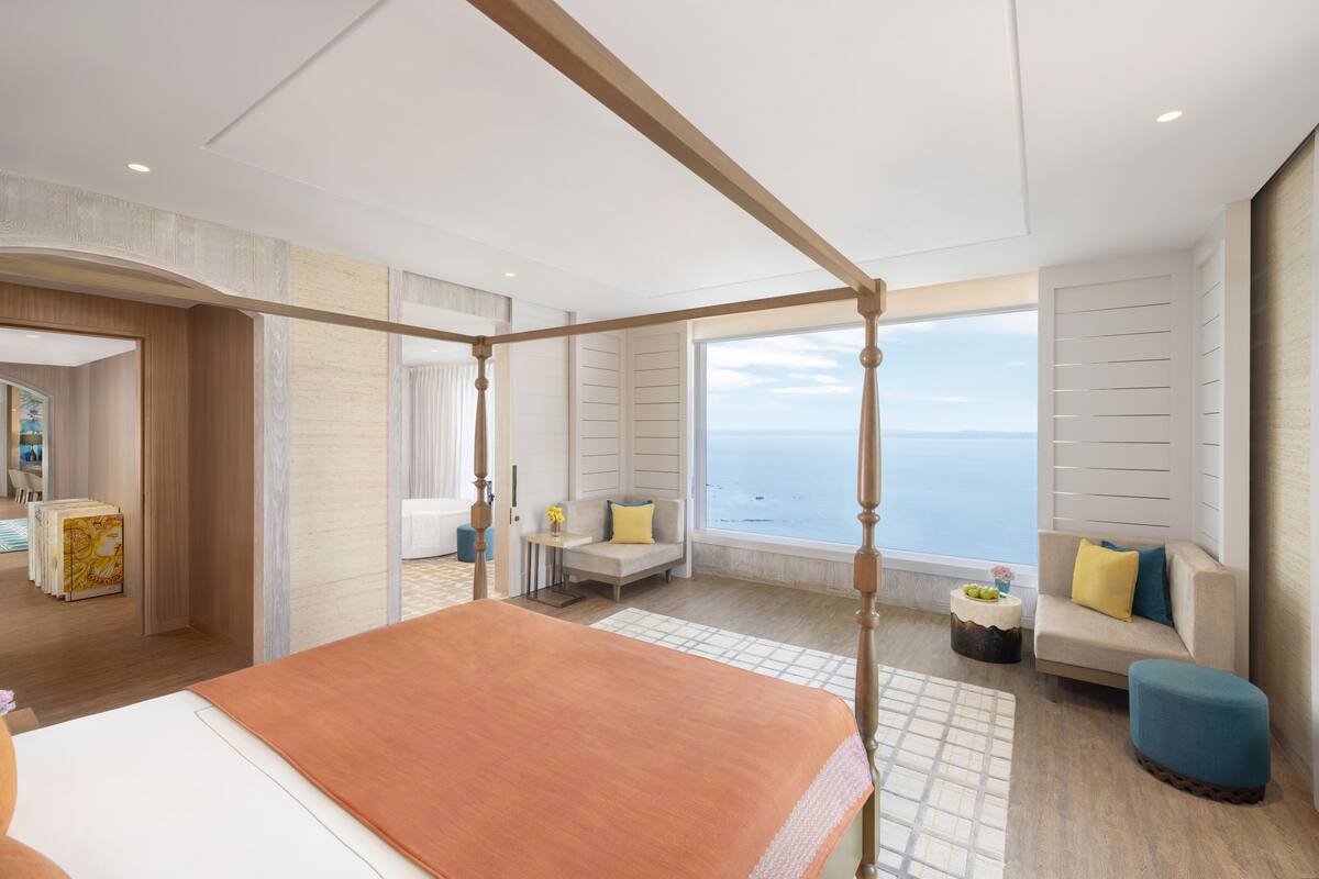 Quarto moderno com cama de dossel, um sofá e vista para o mar.