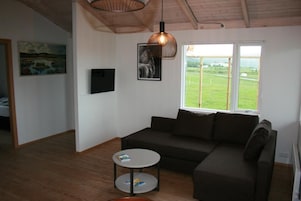 Uma sala de estar moderna com um sofá seccional, uma mesa de centro redonda e uma grande janela com vista para uma paisagem verdejante.