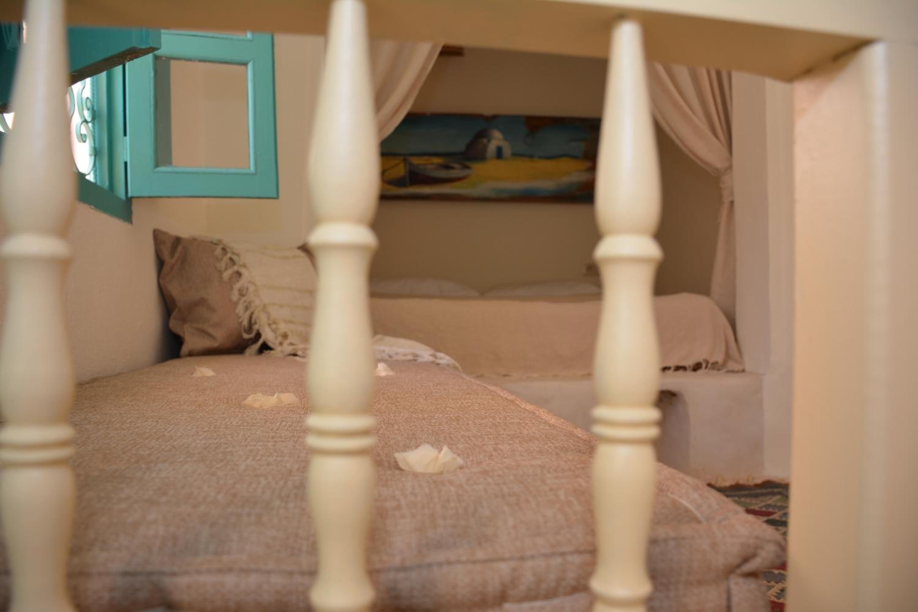 Quarto com uma cama, um quadro na parede e uma janela com moldura azul.