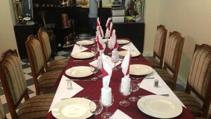 Mesa de jantar posta para refeição, com pratos brancos, talheres e guardanapos vermelhos.
