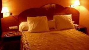 Quarto de hotel com cabeceira de madeira, duas mesas de cabeceira e cama com colcha estampada.