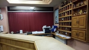 Uma área de recepção com balcão, uma cortina vermelha, um armário de madeira com portas de vidro e um quadro na parede.