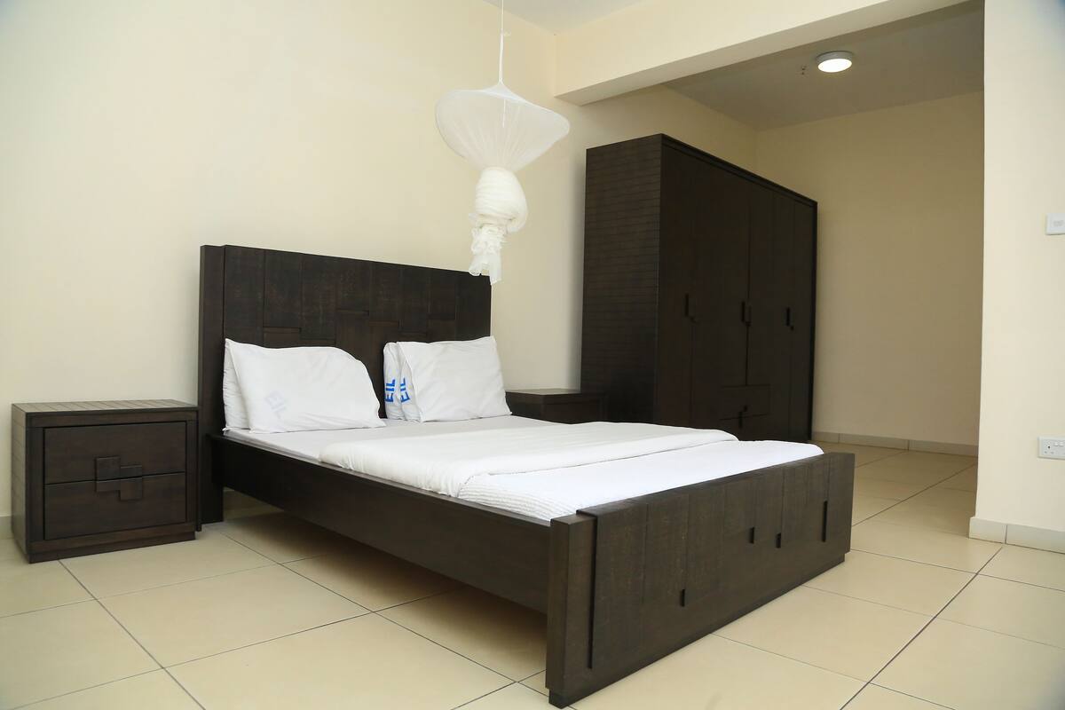 Um quarto com cama, mesa de cabeceira, guarda-roupa e luminária pendente.