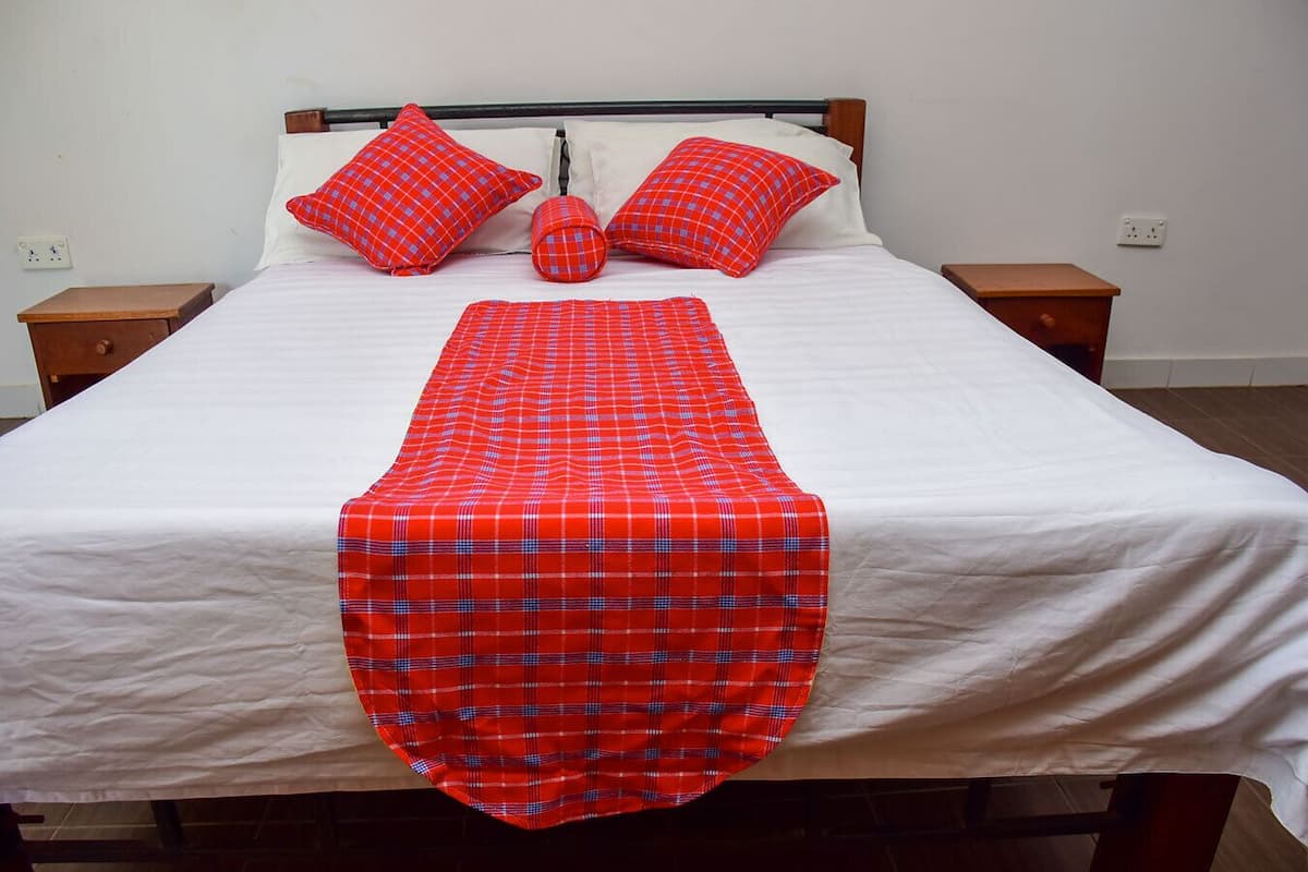 Uma cama com colchão branco e cobre xadrez vermelha. Há duas mesas de cabeceira de madeira de cada lado da cama.