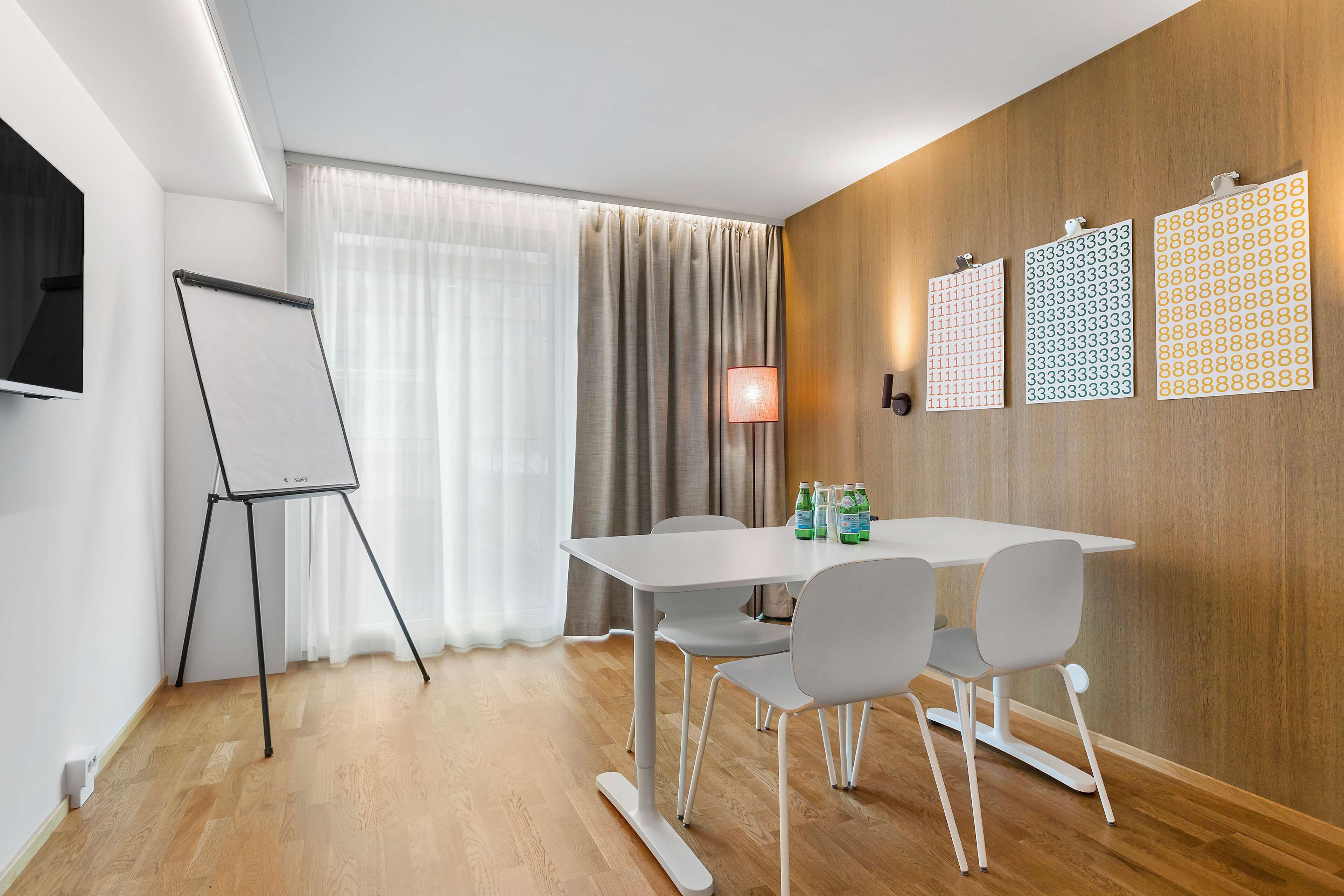 Uma sala de reuniões moderna com uma mesa branca, quatro cadeiras, um flip chart e uma tela de projetor.
