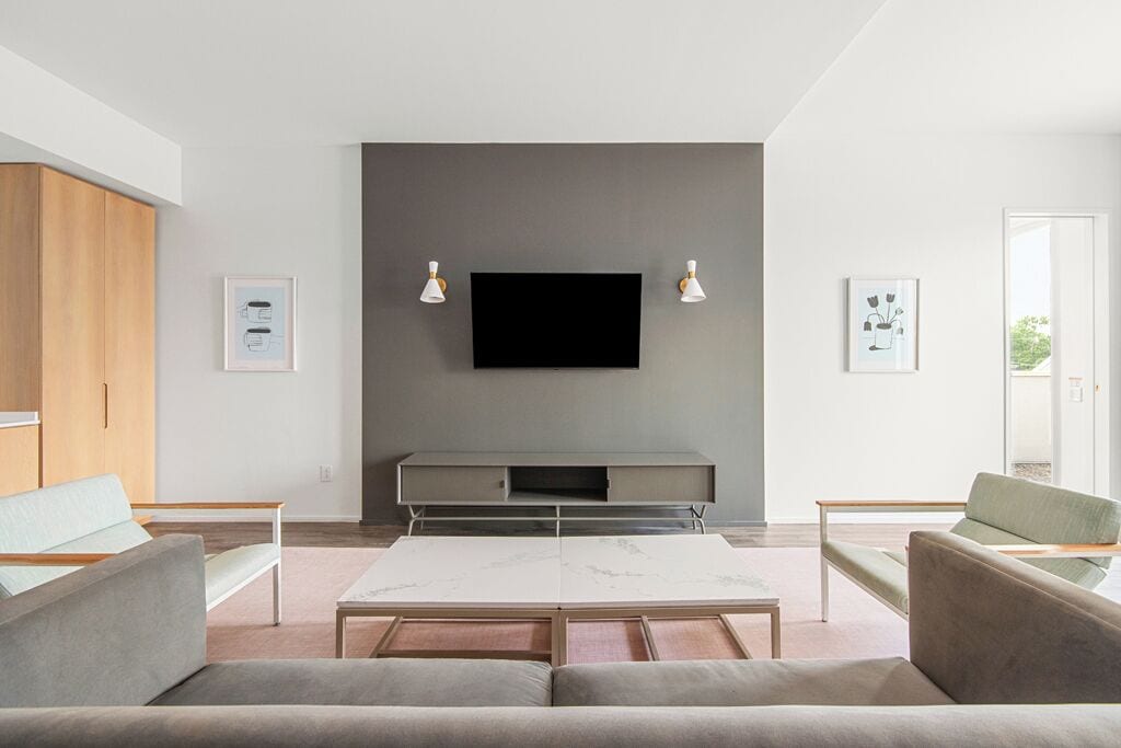 Uma sala de estar moderna com uma televisão de tela plana, duas luminárias fixadas na parede, um sofá, uma mesa de centro e um armário.