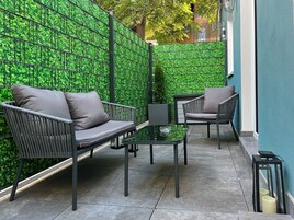 Uma área de pátio com mobiliário de vime, uma mesa de vidro e um muro coberto por folhagem verde.