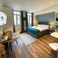 Quarto de hotel com cama, escrivaninha, cadeira, mesinha e televisão.