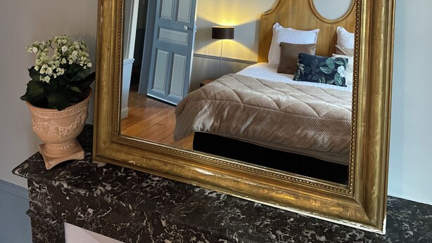 Quarto com um espelho grande e ornamentado, cama com várias almofadas, abajur e luminária pendente.