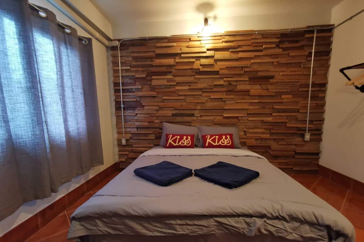 Quarto com parede de madeira, cama com duas almofadas e janela com cortinas.