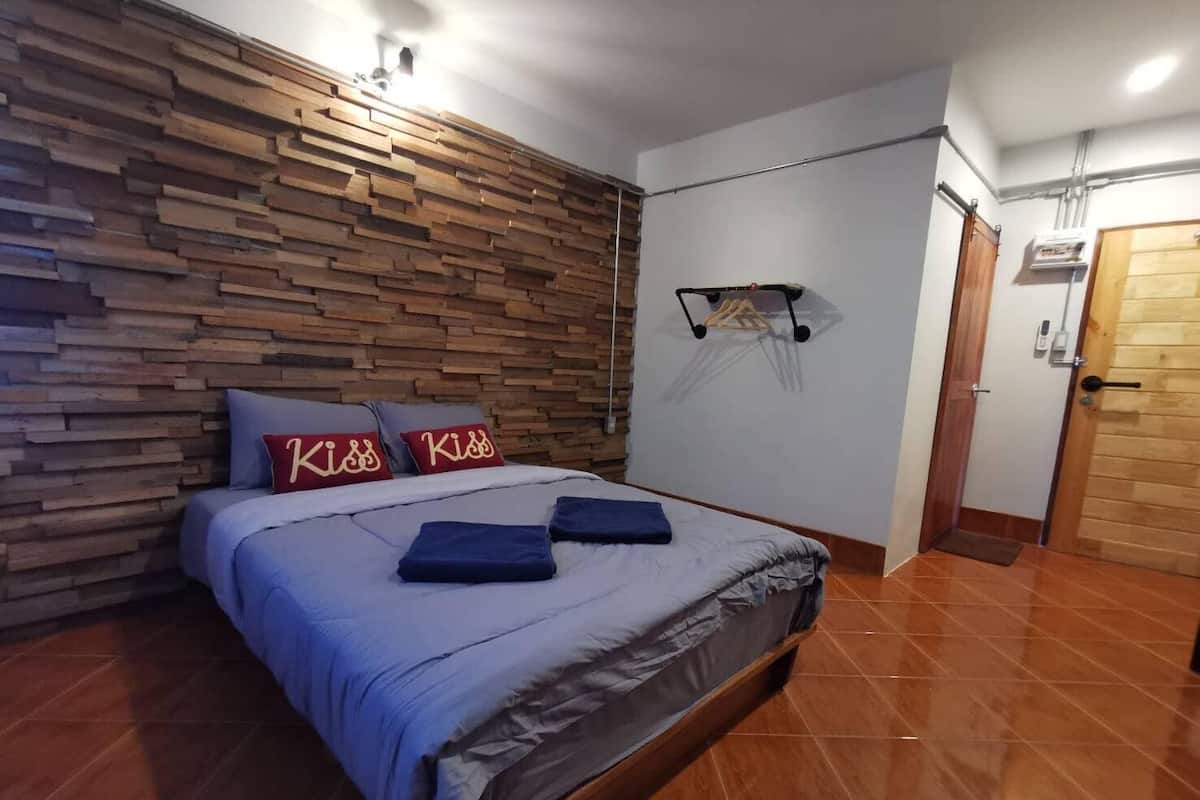 Quarto com cabeceira de madeira, cama com roupa de cama azul e duas almofadas com a inscrição 'Kiss'.