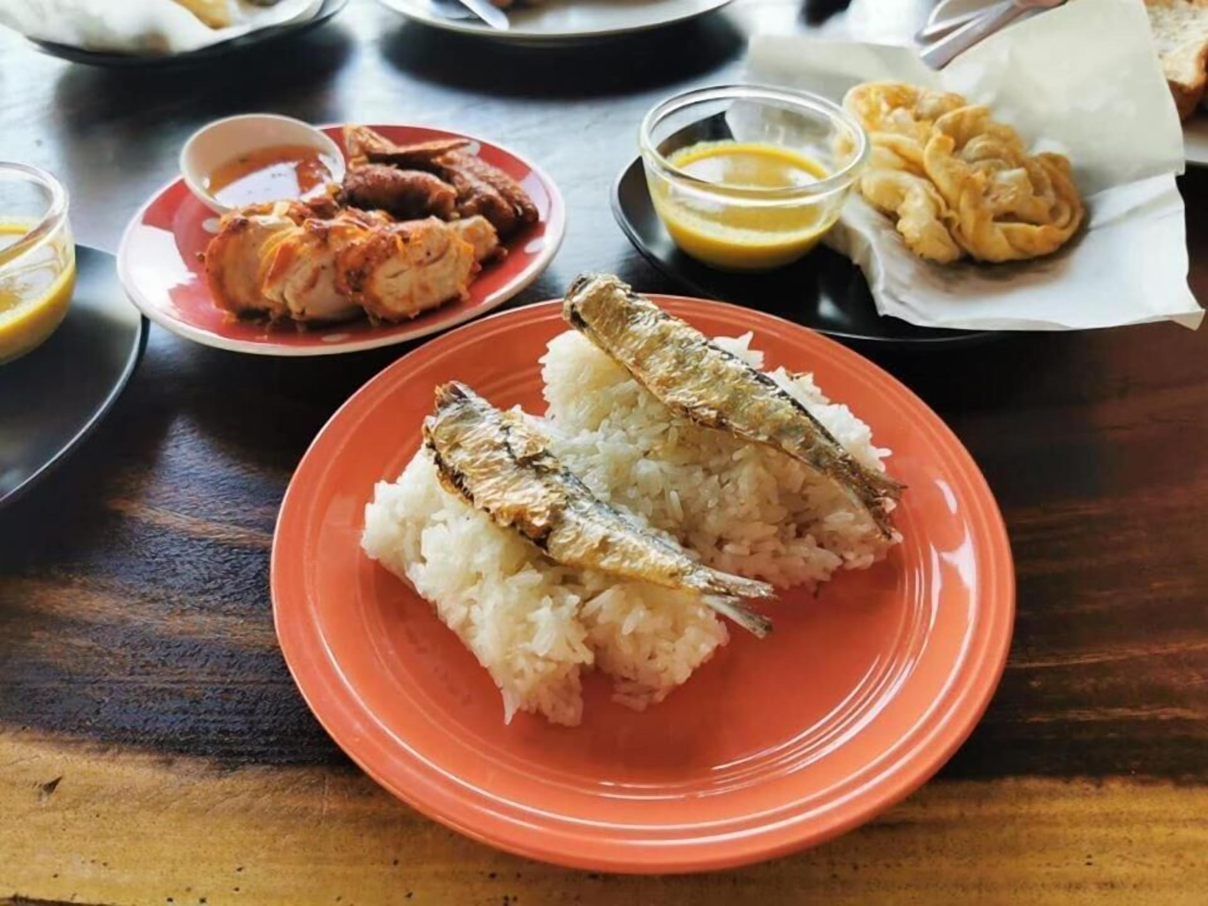 Uma mesa com um prato de peixe frito e arroz, um prato de frango grelhado e uma tigela de molho.