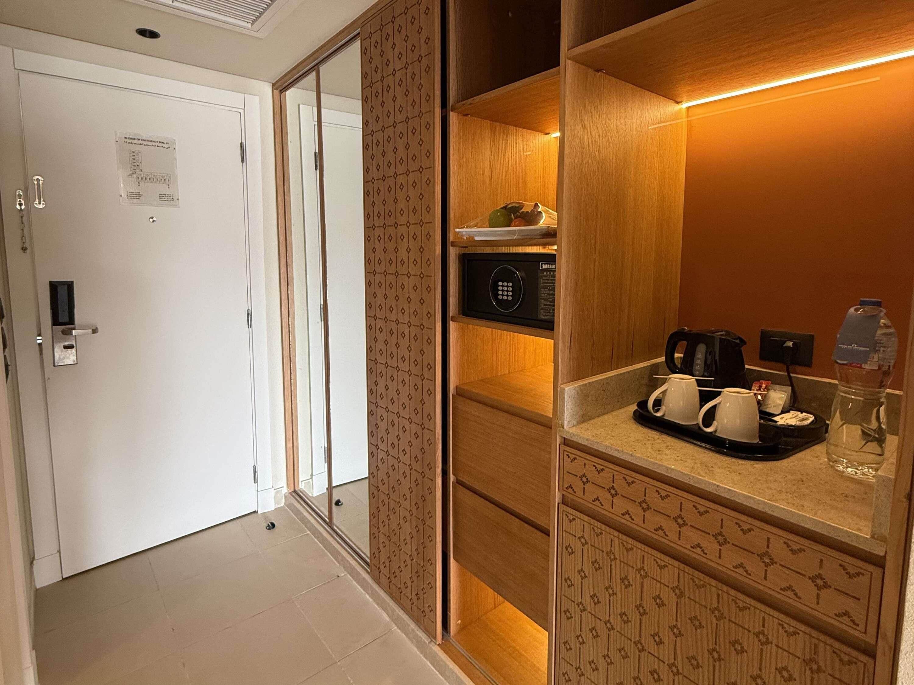 Quarto de hotel com porta de correr, micro-ondas, bandeja com copos e garrafa, e dispensador de água.