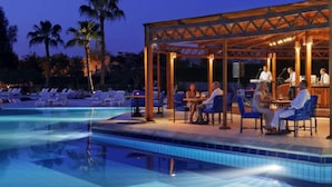 Área da piscina com espreguiçadeiras e um espaço coberto para sentar com uma banda tocando.