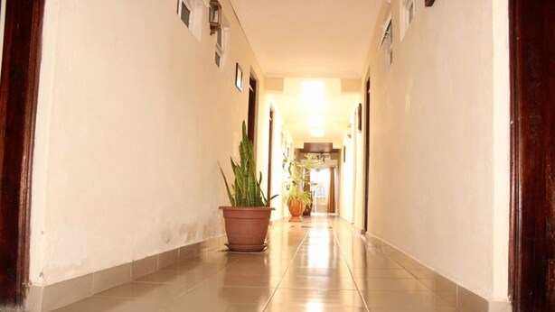 Um corredor com piso ladrilhado, plantas em vasos e portas que dão para os quartos.