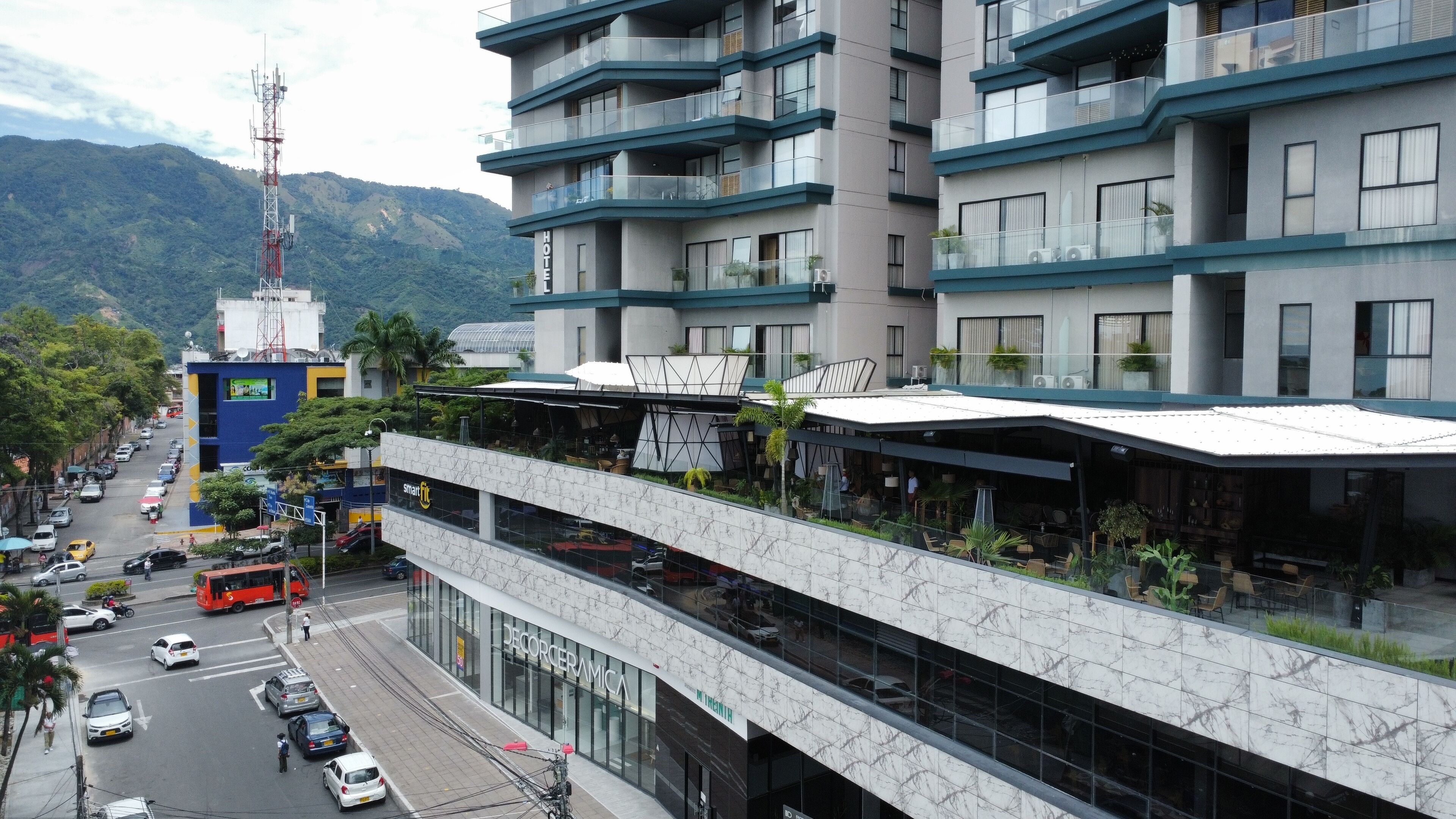Um hotel moderno com vários andares, áreas de estar ao ar livre e vista para uma rua movimentada com carros e um ônibus.