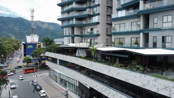 Um hotel moderno com vários andares, áreas de estar ao ar livre e vista para uma rua movimentada com carros e um ônibus.