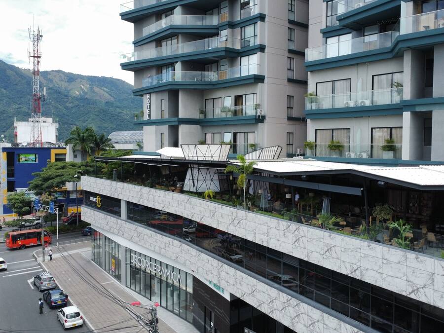 Um hotel moderno com vários andares, áreas de estar ao ar livre e vista para uma rua movimentada com carros e um ônibus.