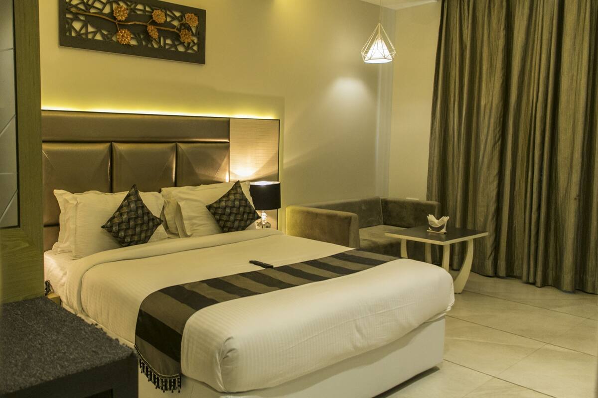 Quarto de hotel moderno com uma cama grande, uma mesinha, uma cadeira e uma peça decorativa na parede.