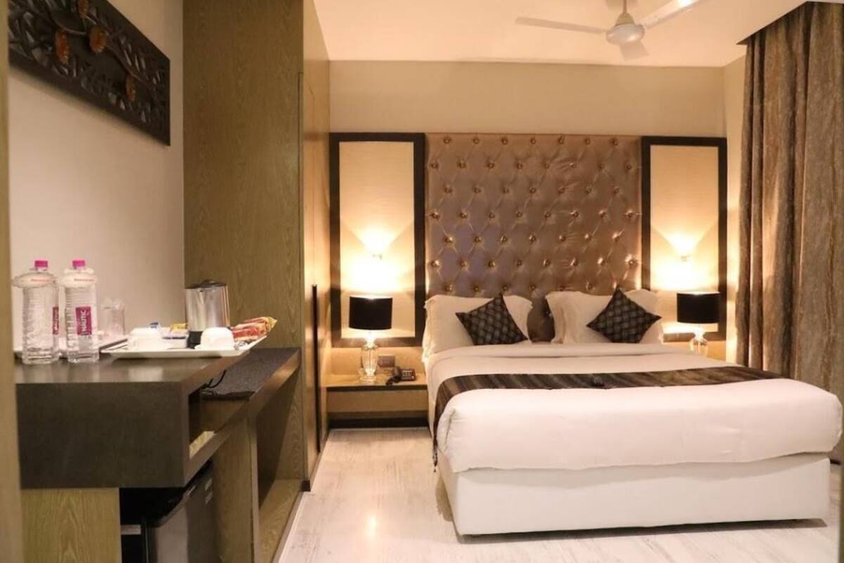 Quarto de hotel com uma cama grande, duas mesas de cabeceira com luminárias, uma escrivaninha com artigos de higiene e um ventilador de teto.