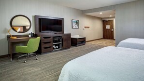 Quarto de hotel com uma cama, uma escrivaninha com cadeira, uma televisão e um pequeno armário.