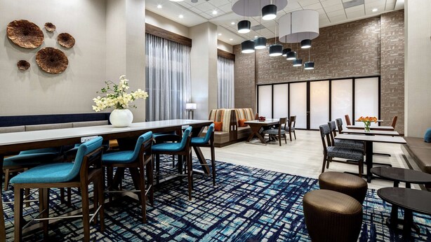 Um hall de hotel com um balcão de recepção extenso, área de estar e uma grande janela com cortinas.