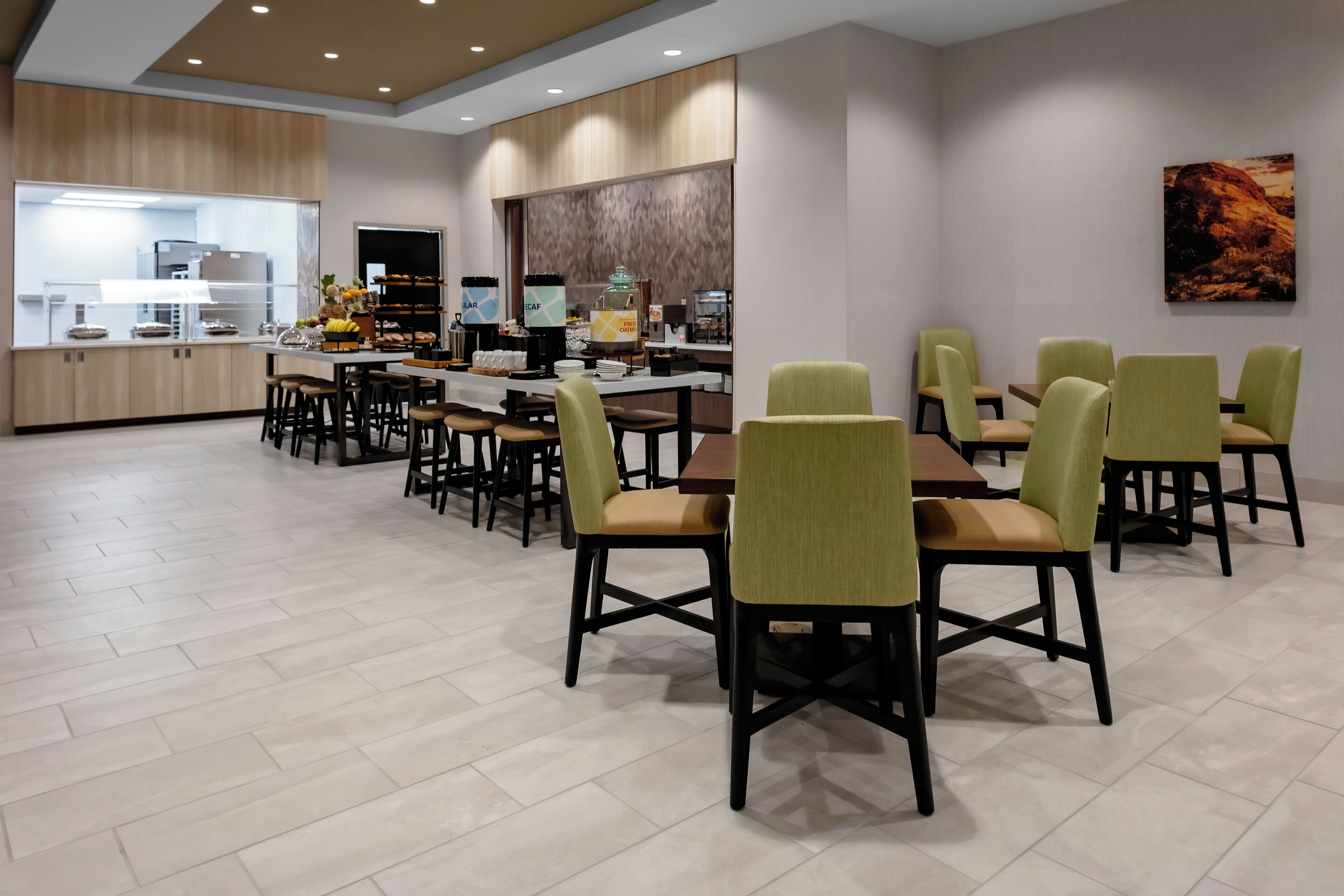 Uma sala de jantar moderna com várias mesas e cadeiras, uma cozinha ao fundo e uma janela grande.